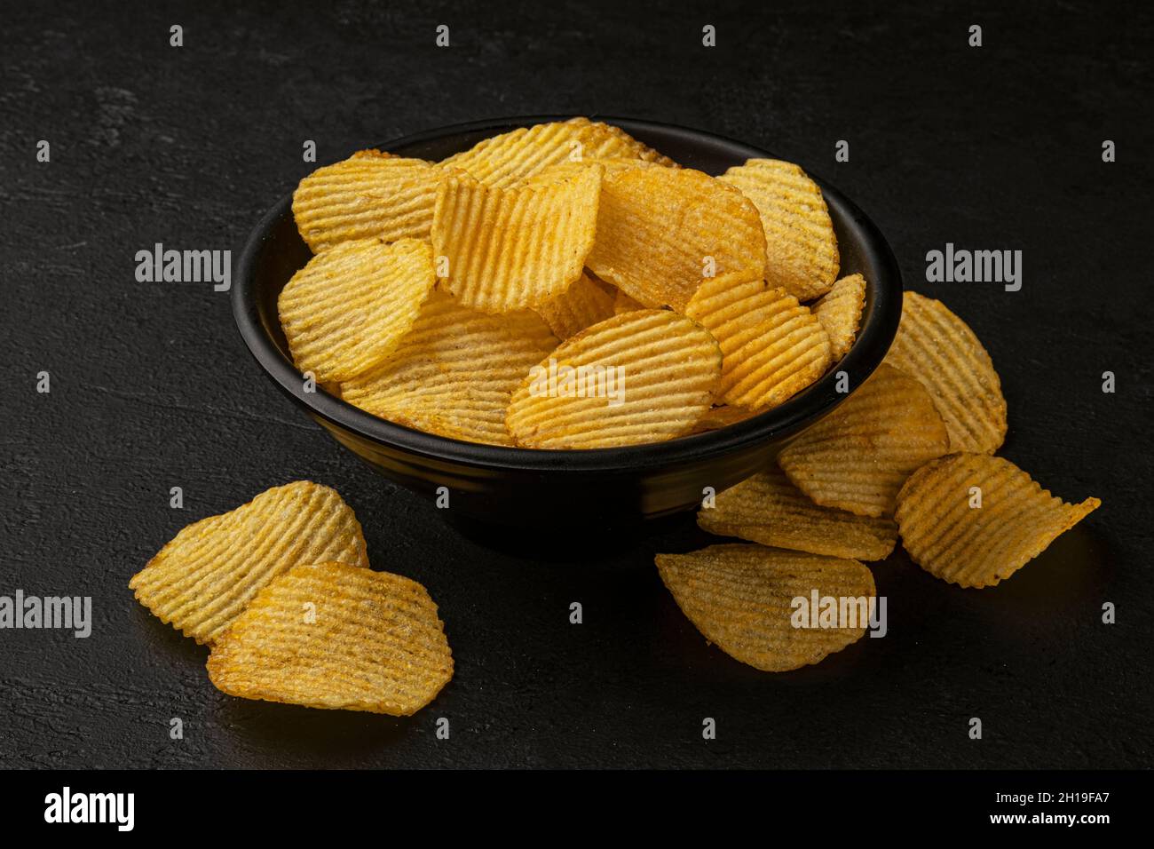 Ridged potato chips on black background Stock Photo - Alamy