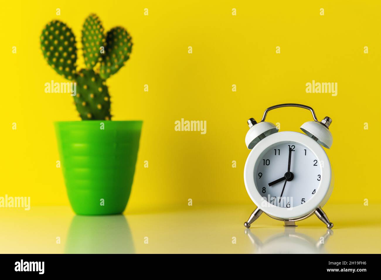 White alarm clock with cactus in pot on wooden desk. Minimal time ...