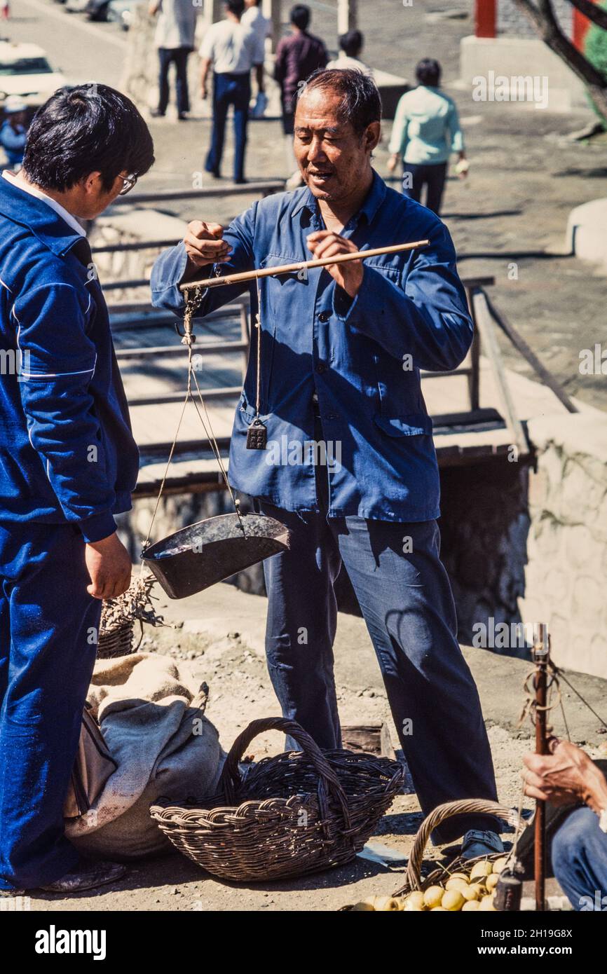 A vendor weighing produce with a hand balance scale in the farmers ...
