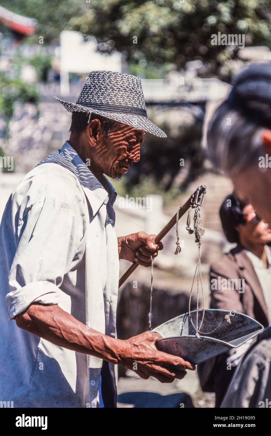 A vendor weighing produce with a hand balance scale in the farmers ...