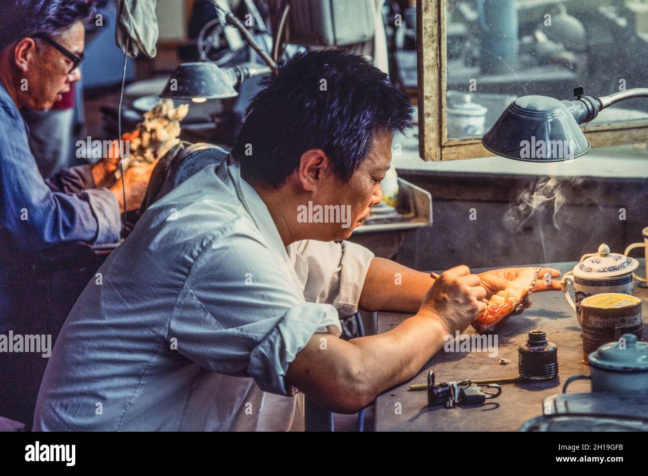 An artisan in a jade factory works on a jade figurine whlie smoking a ...