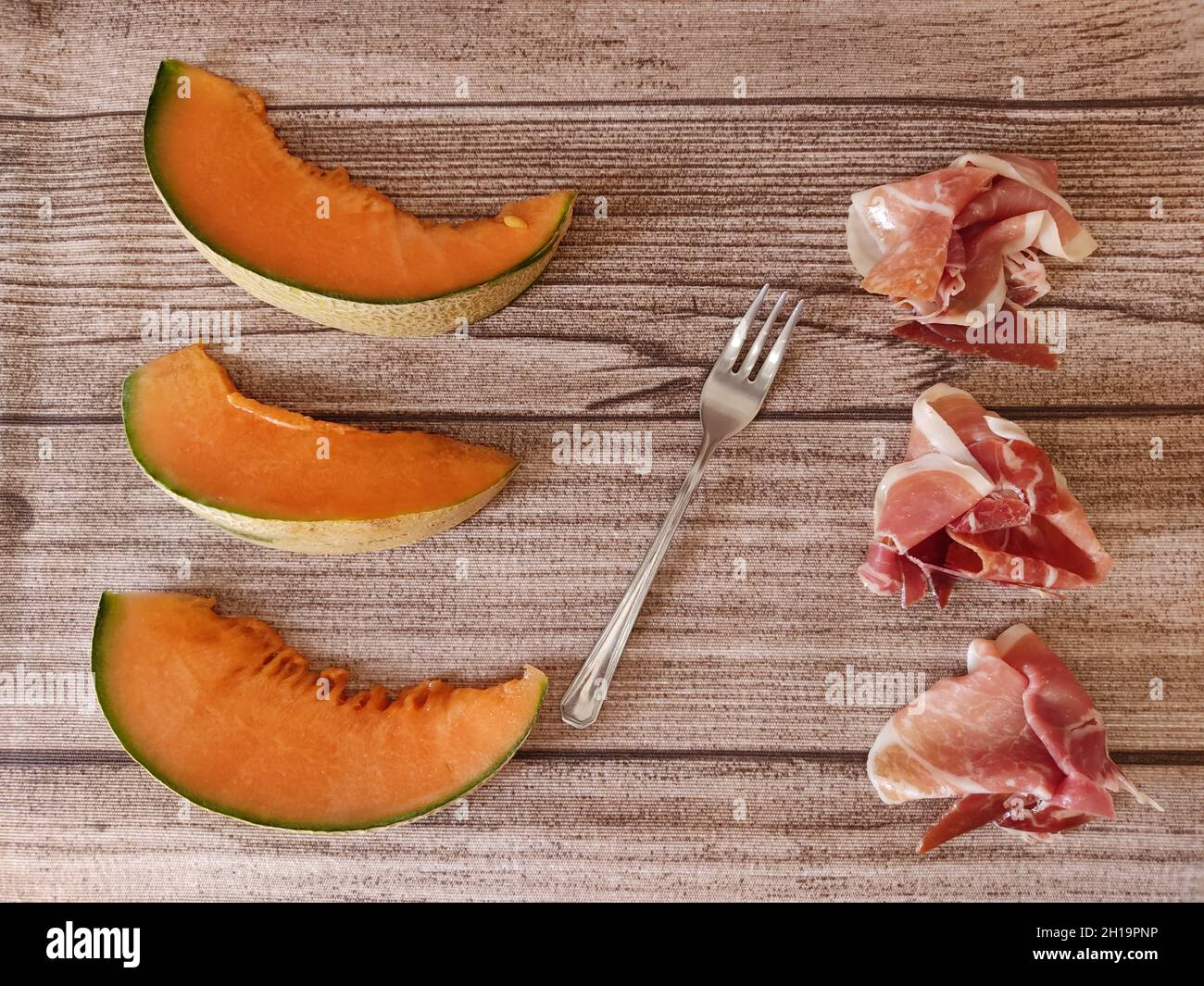The flat lay of melon and bacon pieces on the wooden table; ingredients ...