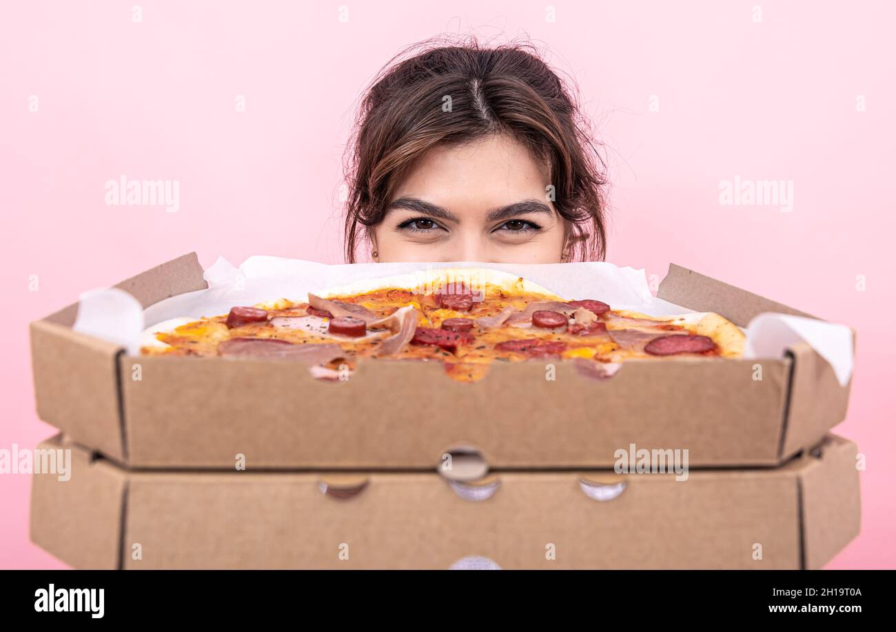 Attractive girl holding pizza in a cardboard box on a pink background ...