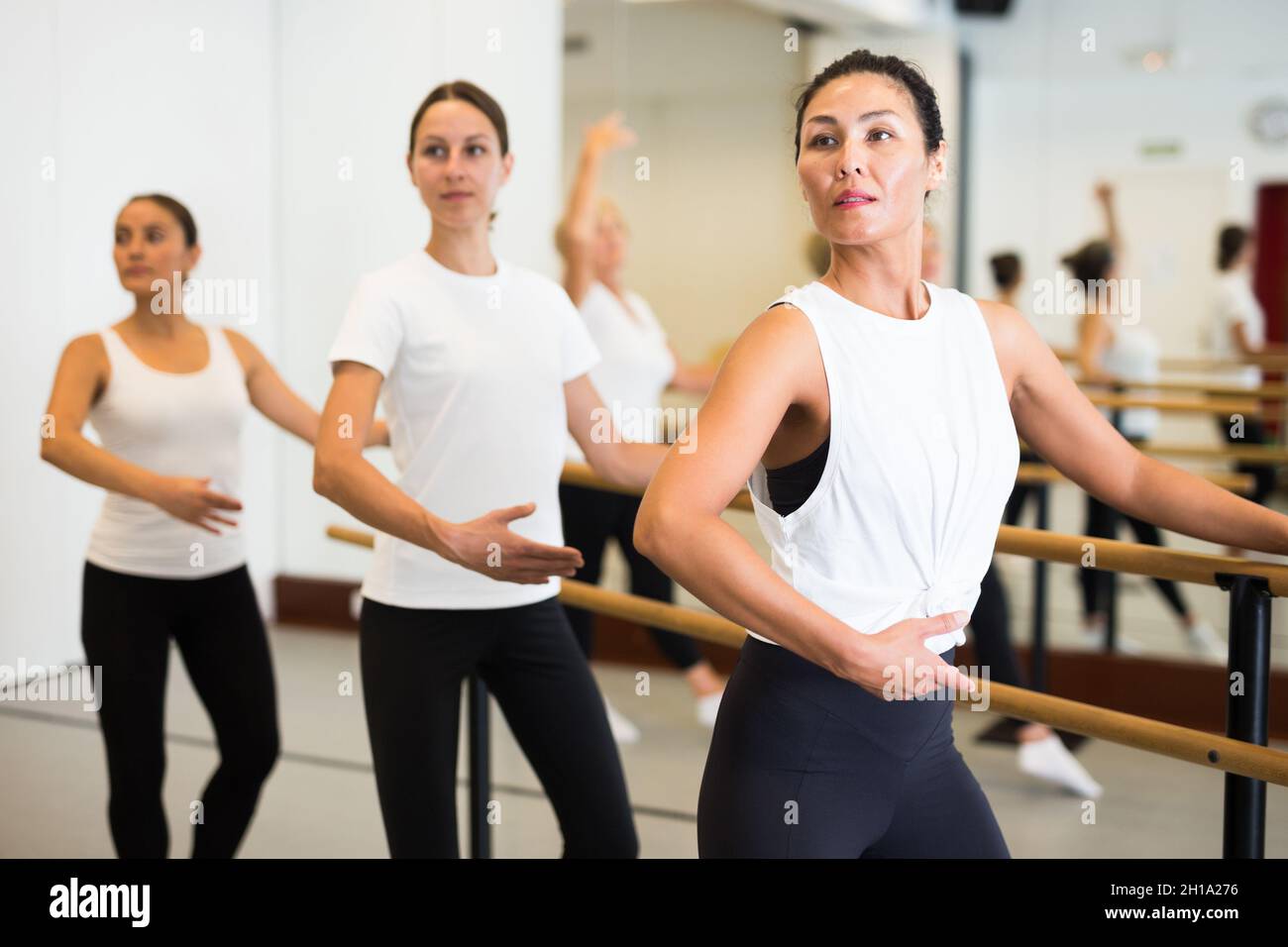Dancing Asian woman perform demi plie near the ballet barre, standing ...