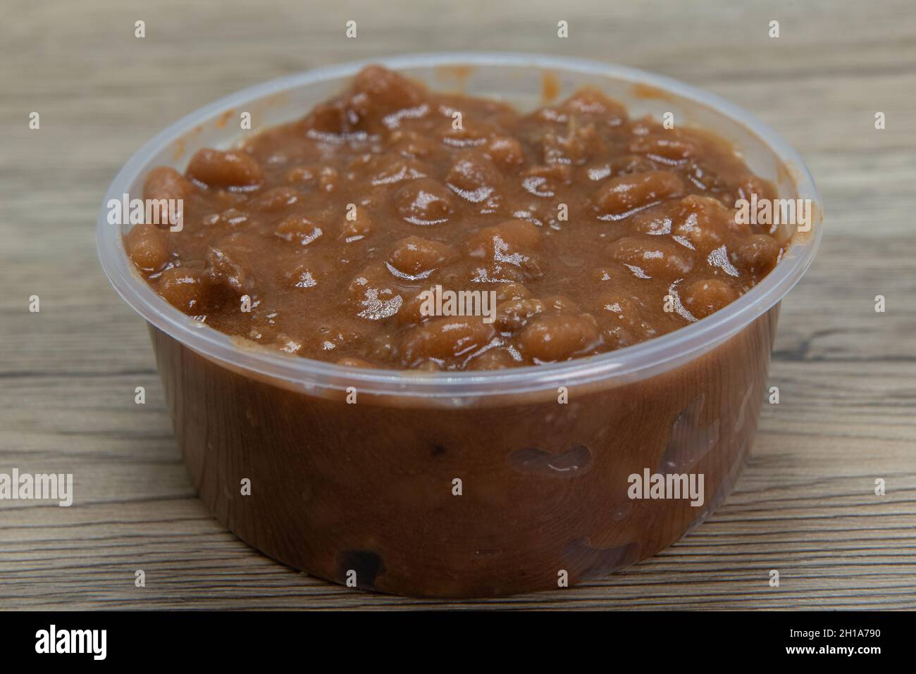 Generous portion side order of baked beans in a clear plastic bowl to ...