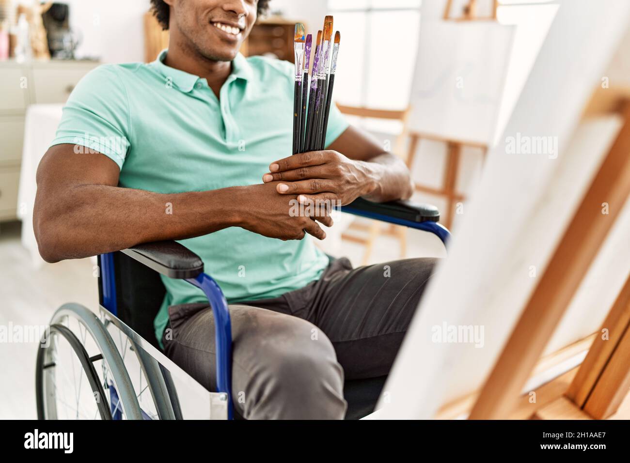 Young african american disabled artist man holding paintbrushes sitting ...