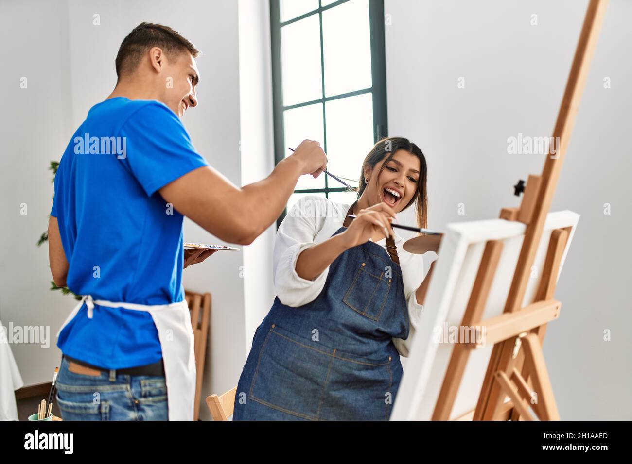 Two students smiling happy playing with paintbrush painting to each ...