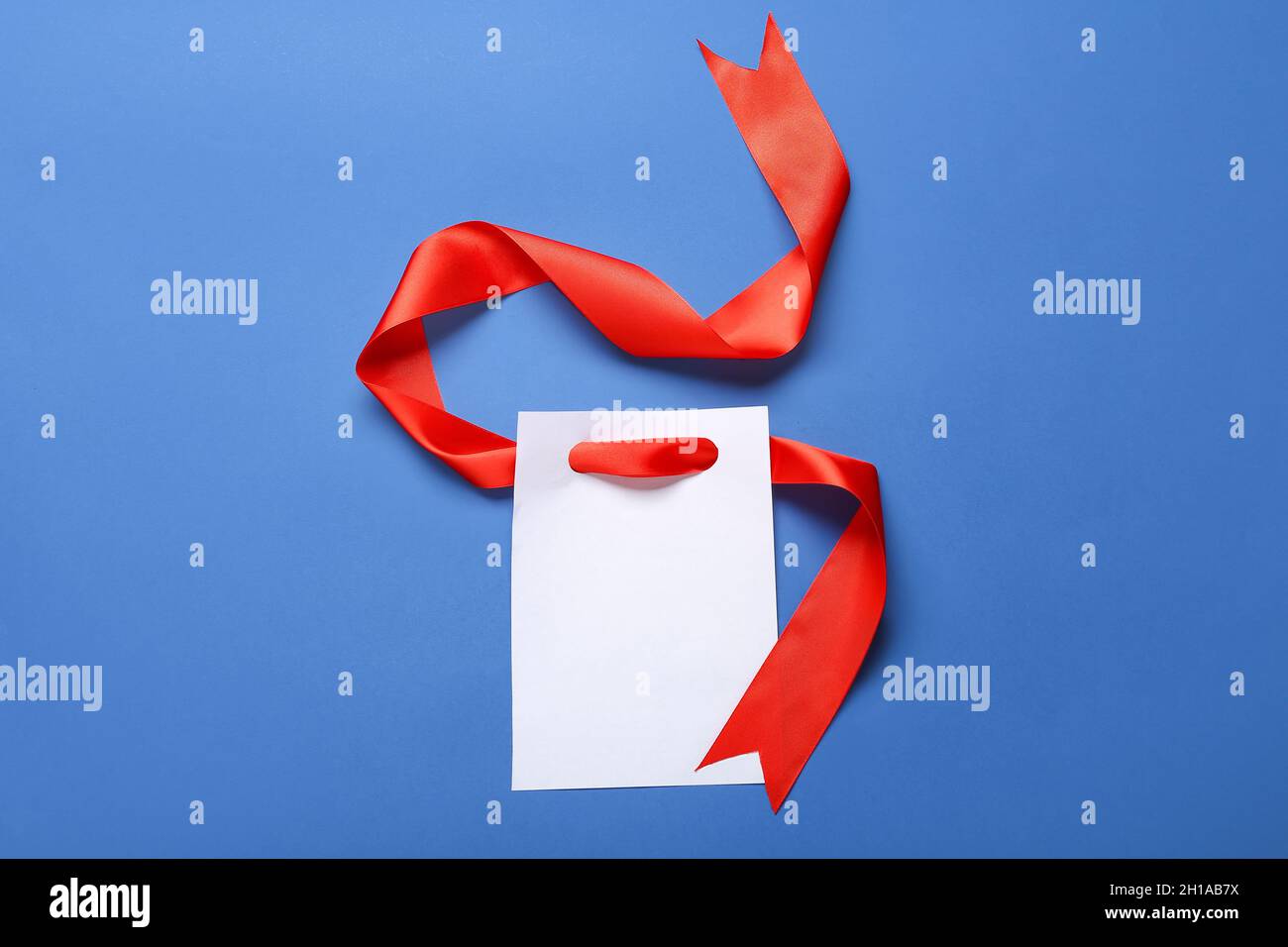 Paper tag with red ribbon on color background Stock Photo - Alamy
