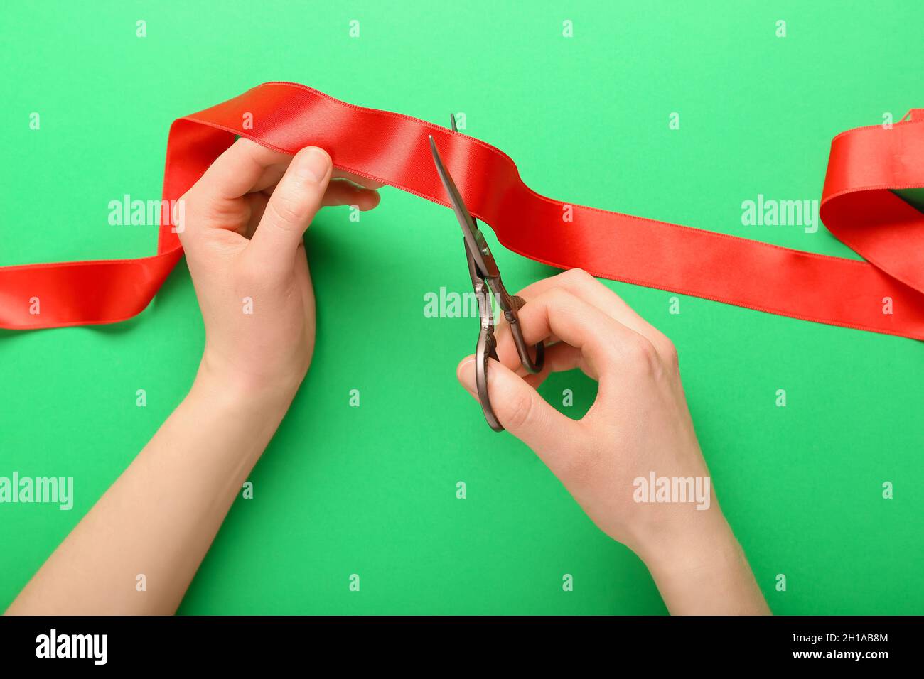 Woman cutting red ribbon on green background Stock Photo - Alamy