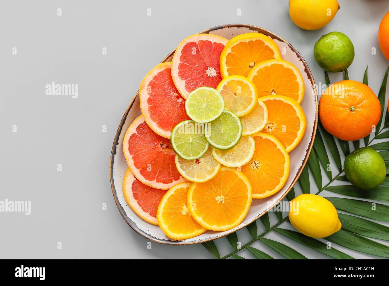 Plate of different citrus fruits and palm leaf on grey background Stock ...