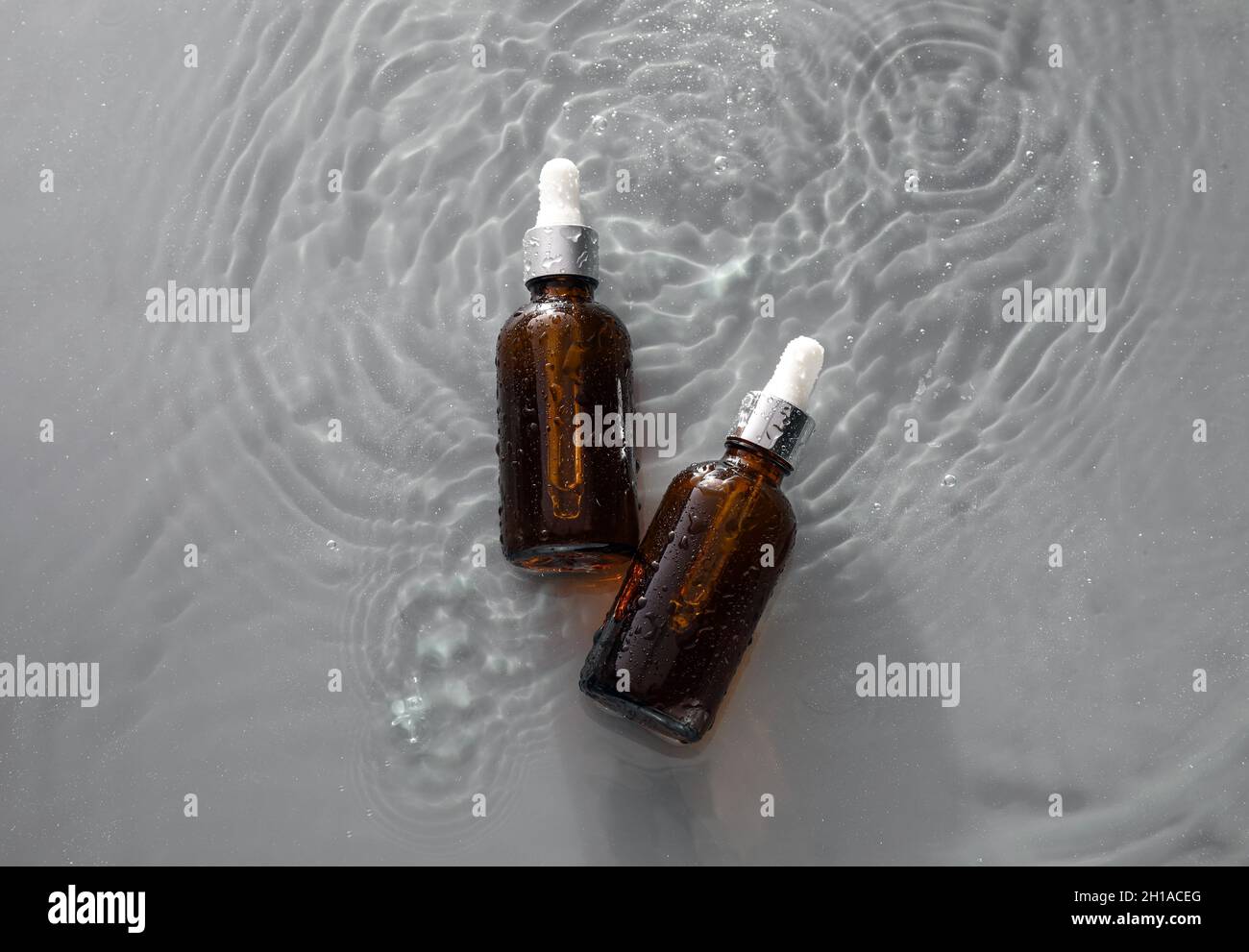 Cosmetic dropper bottles in water on grey background Stock Photo - Alamy
