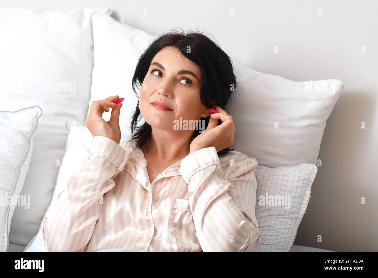 Mature woman putting pink ear plugs on bed Stock Photo - Alamy