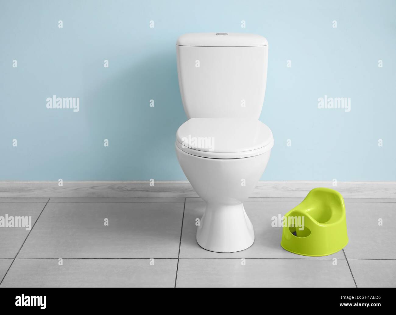 Potty and toilet bowl on tile floor near color wall Stock Photo - Alamy