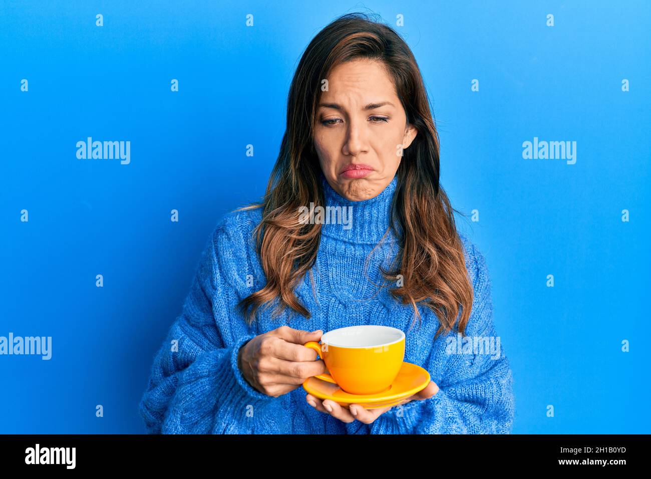 Young latin woman drinking a cup of coffee depressed and worry for ...