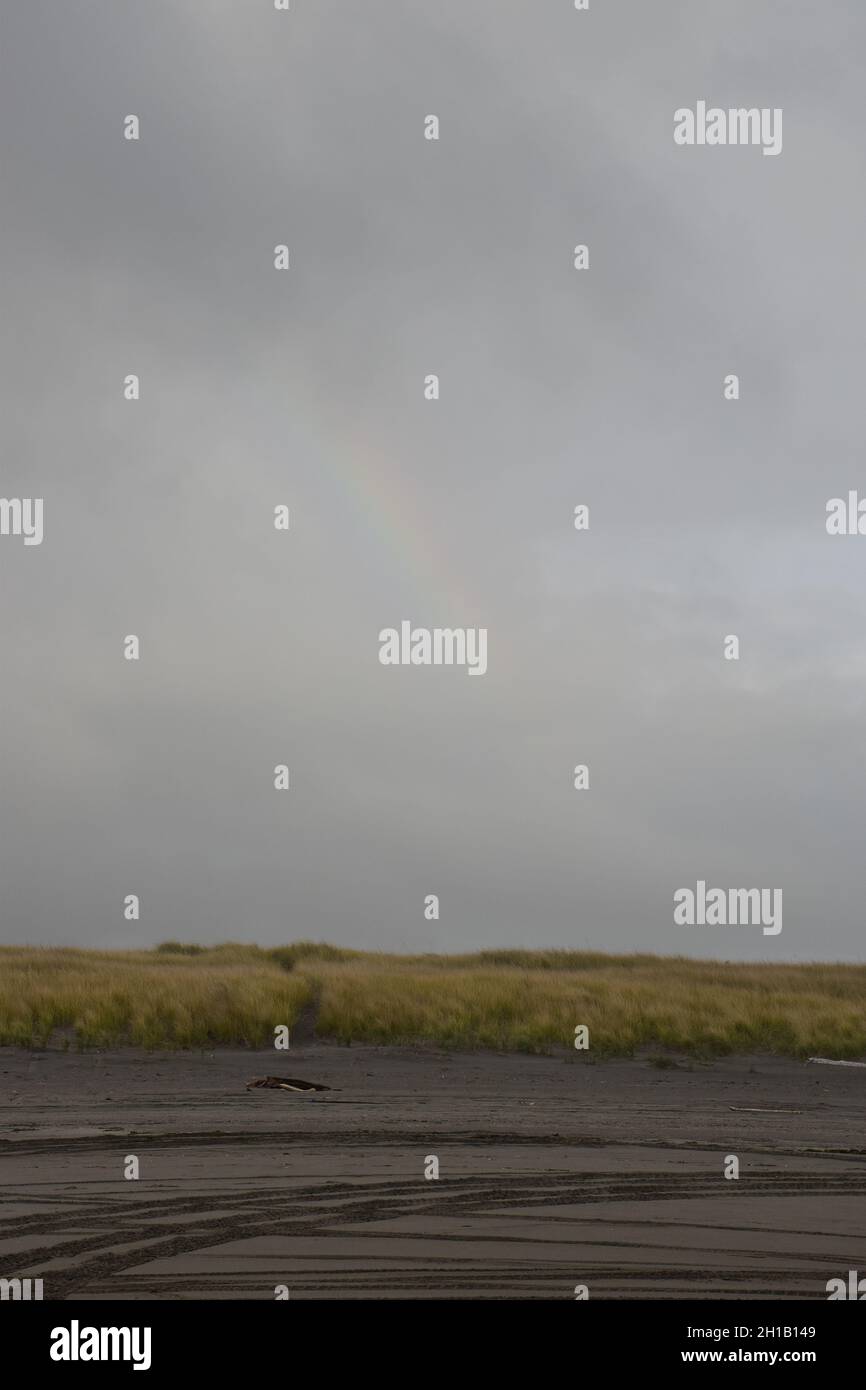 A faint rainbow in a cloudy sky over sand dunes on the Long Beach ...