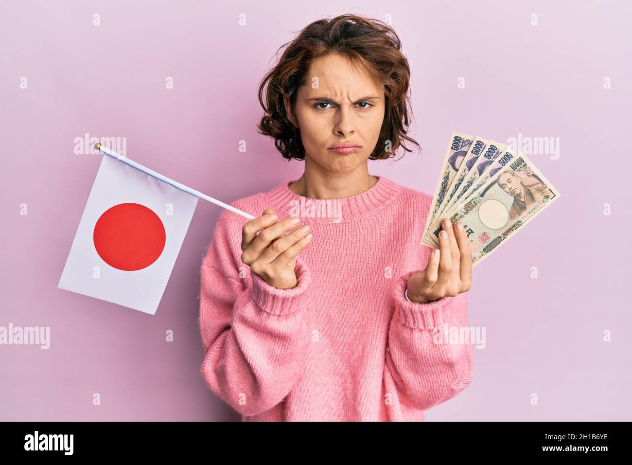Young brunette woman holding japan flag and yen banknotes depressed and ...