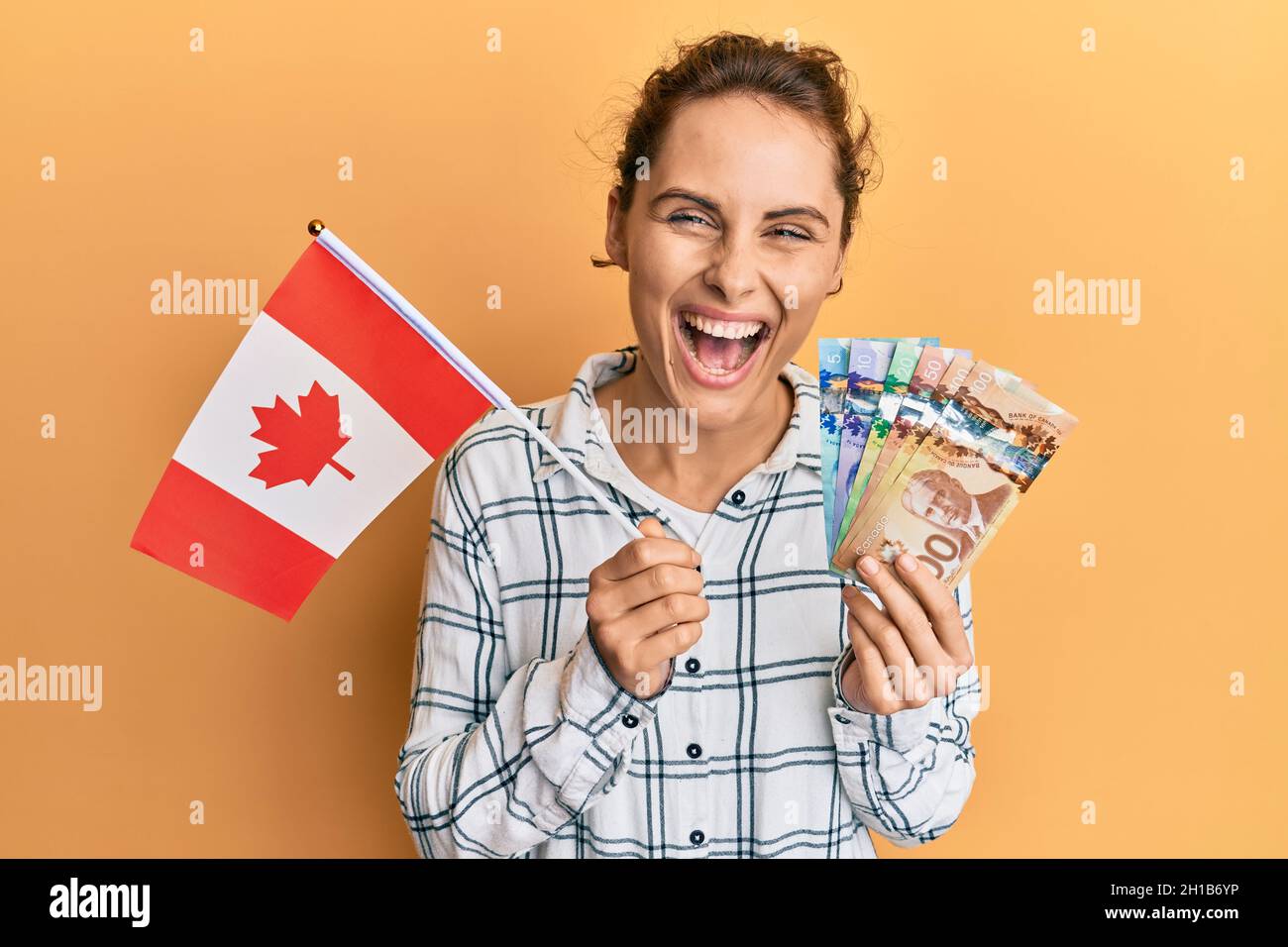 Young brunette woman holding canada flag and dollars smiling and ...