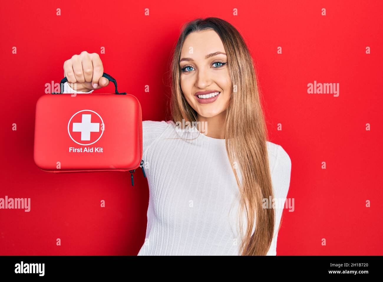 Young blonde girl holding first aid kit looking positive and happy ...