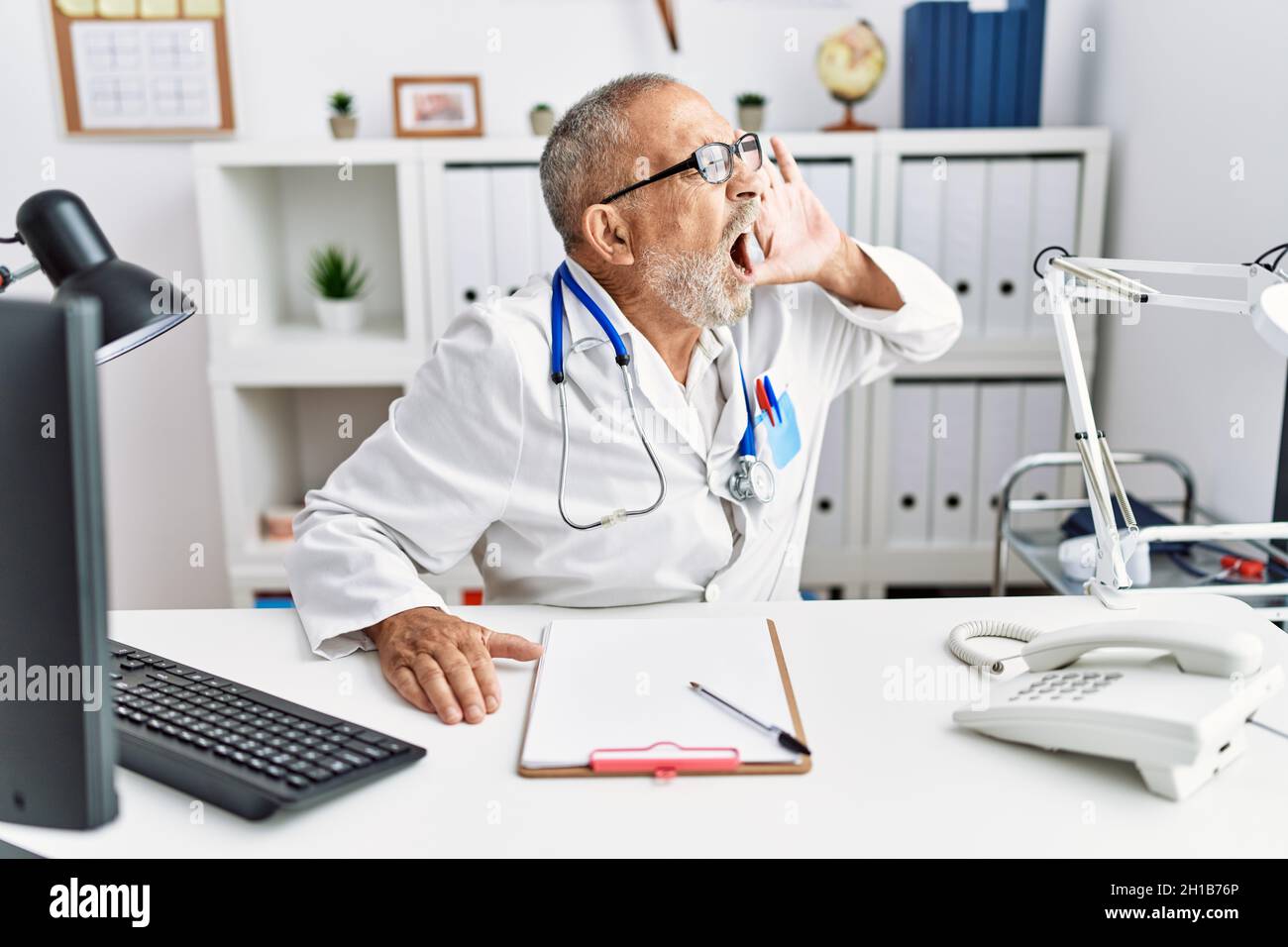 Mature doctor man at the clinic shouting and screaming loud to side ...