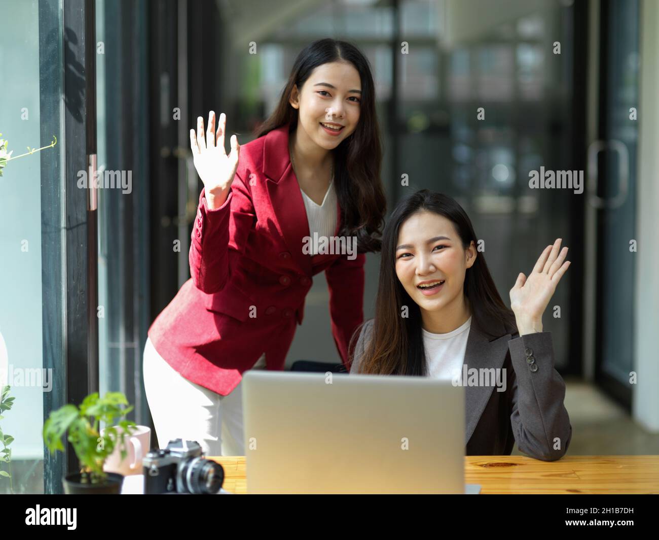 Two happy friendly businesswomen hand greeting gesture to camera in the ...