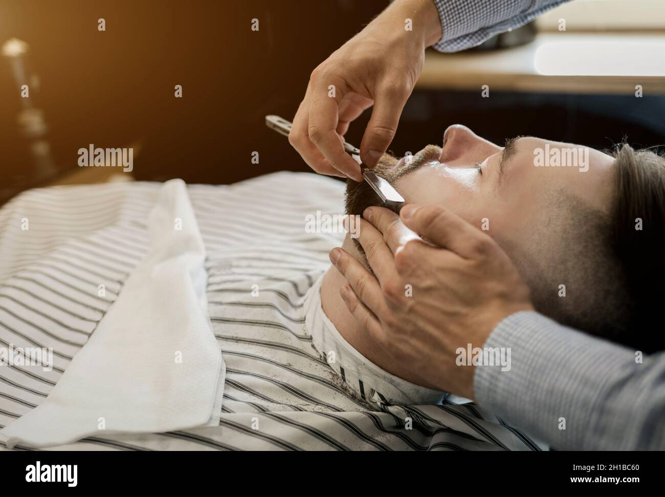 barber shaving a man with a sharp steel razor. concept of barbershop ...