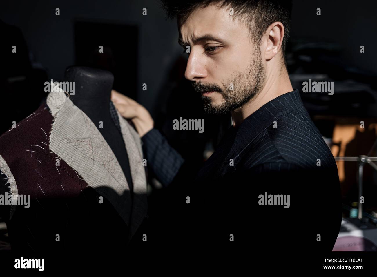 Handsome serious tailor in suit working in atelier with mannequin Stock ...