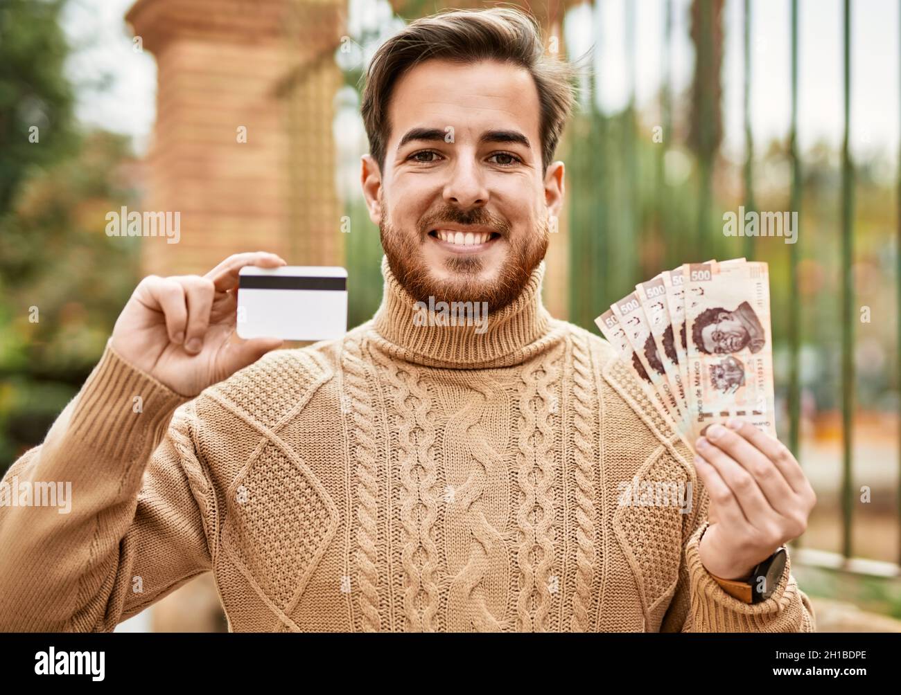 Young caucasian man holding mexican pesos banknotes and credit card at ...