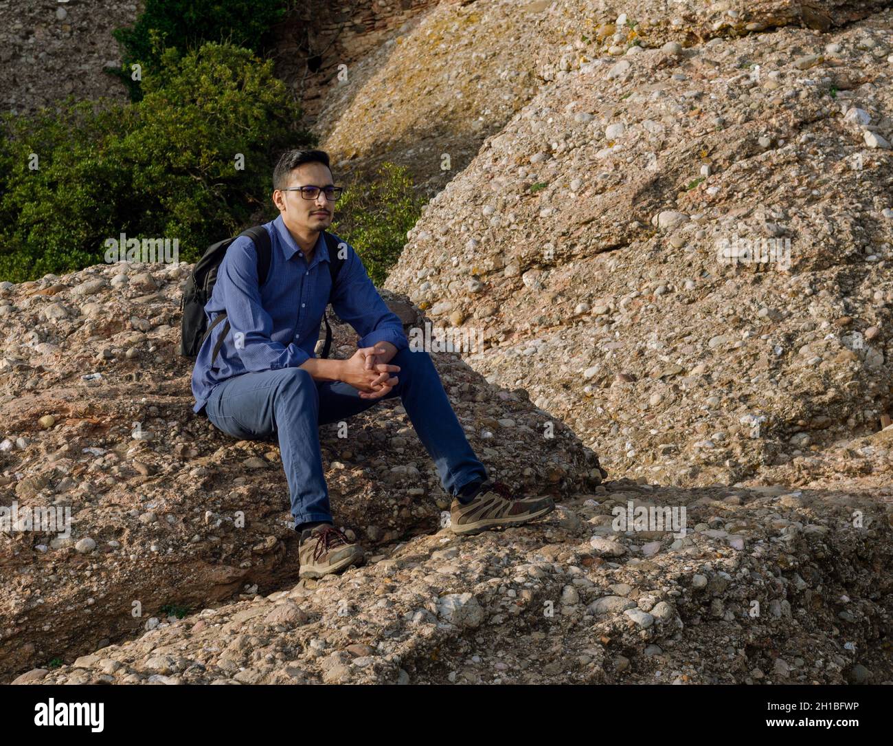 Young indian man with backpack sitting on rock looking at nature around ...