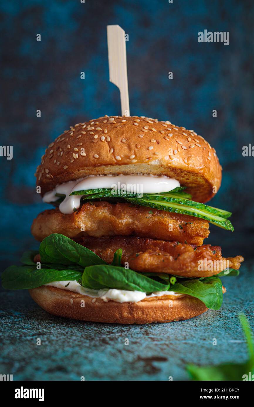 Fish burger on gray plate, dark blue background. Cod fish in batter ...
