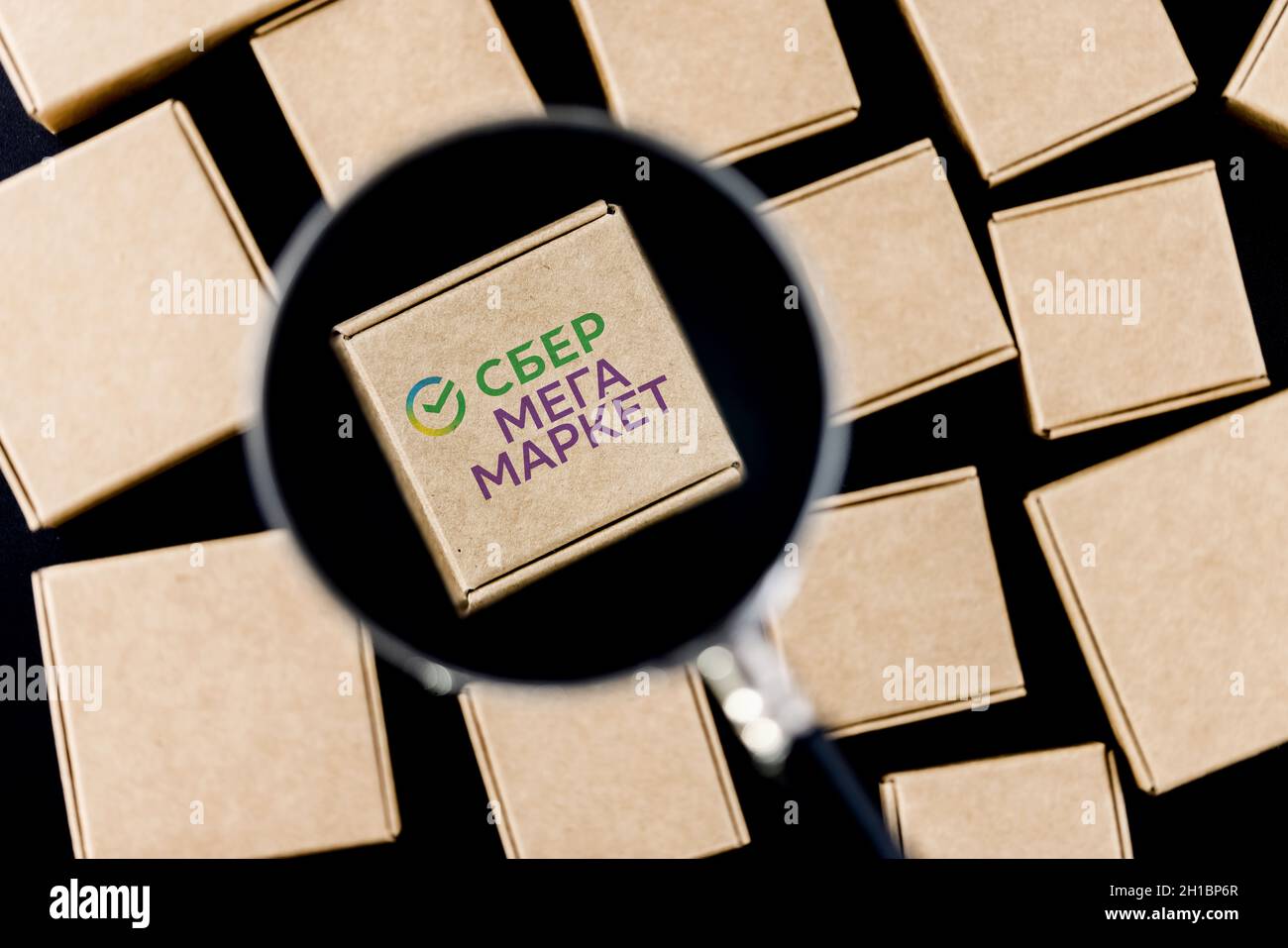 Modified photo of SberMegaMarket logo on a box under a magnifying glass ...