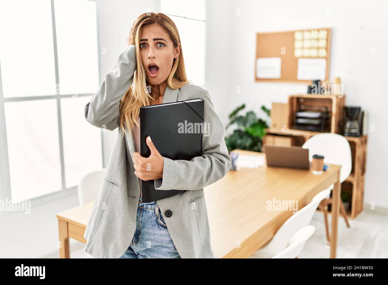 Blonde business woman at the office crazy and scared with hands on head ...