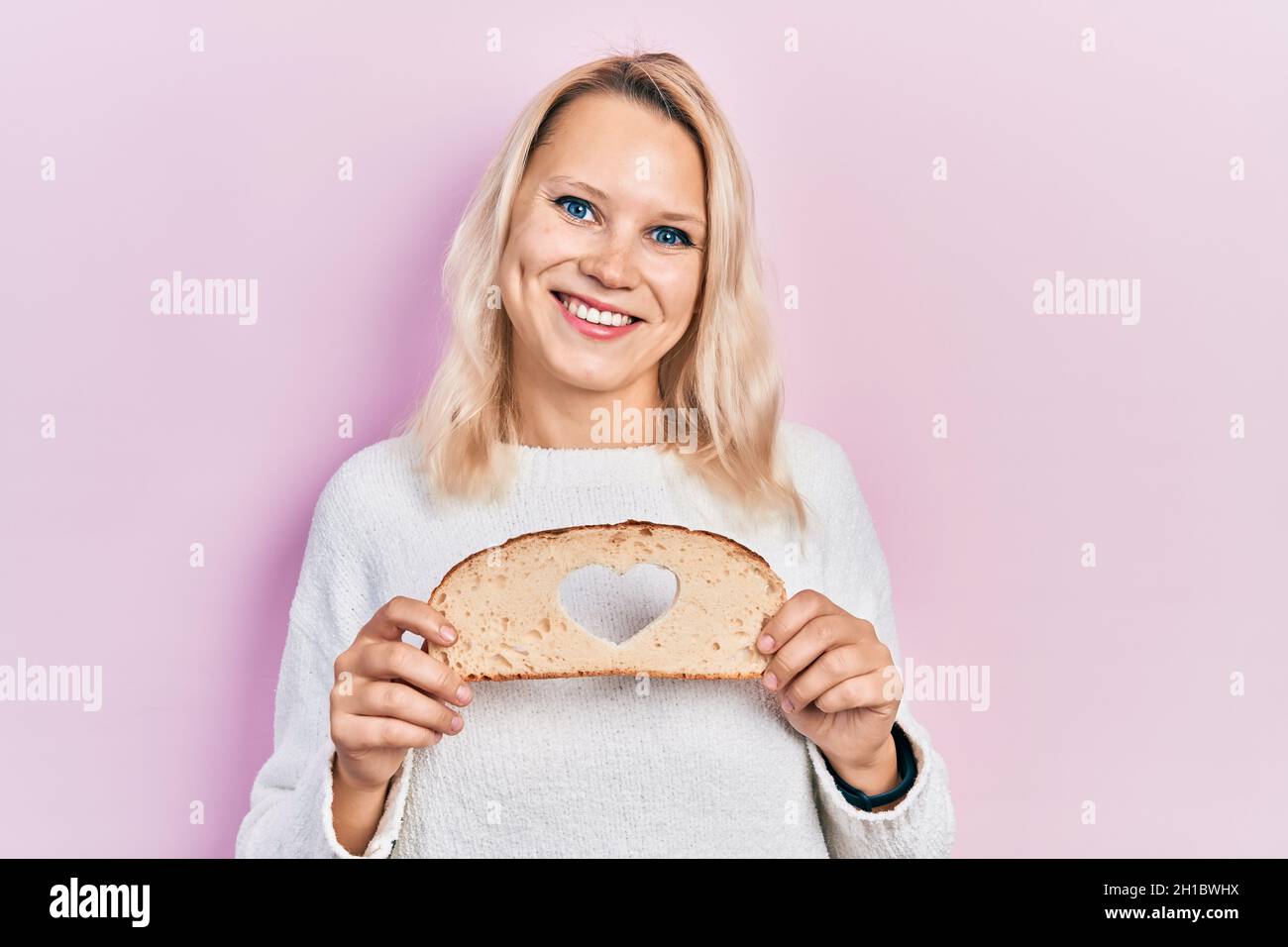 Beautiful caucasian blonde woman holding bread loaf with heart shape ...