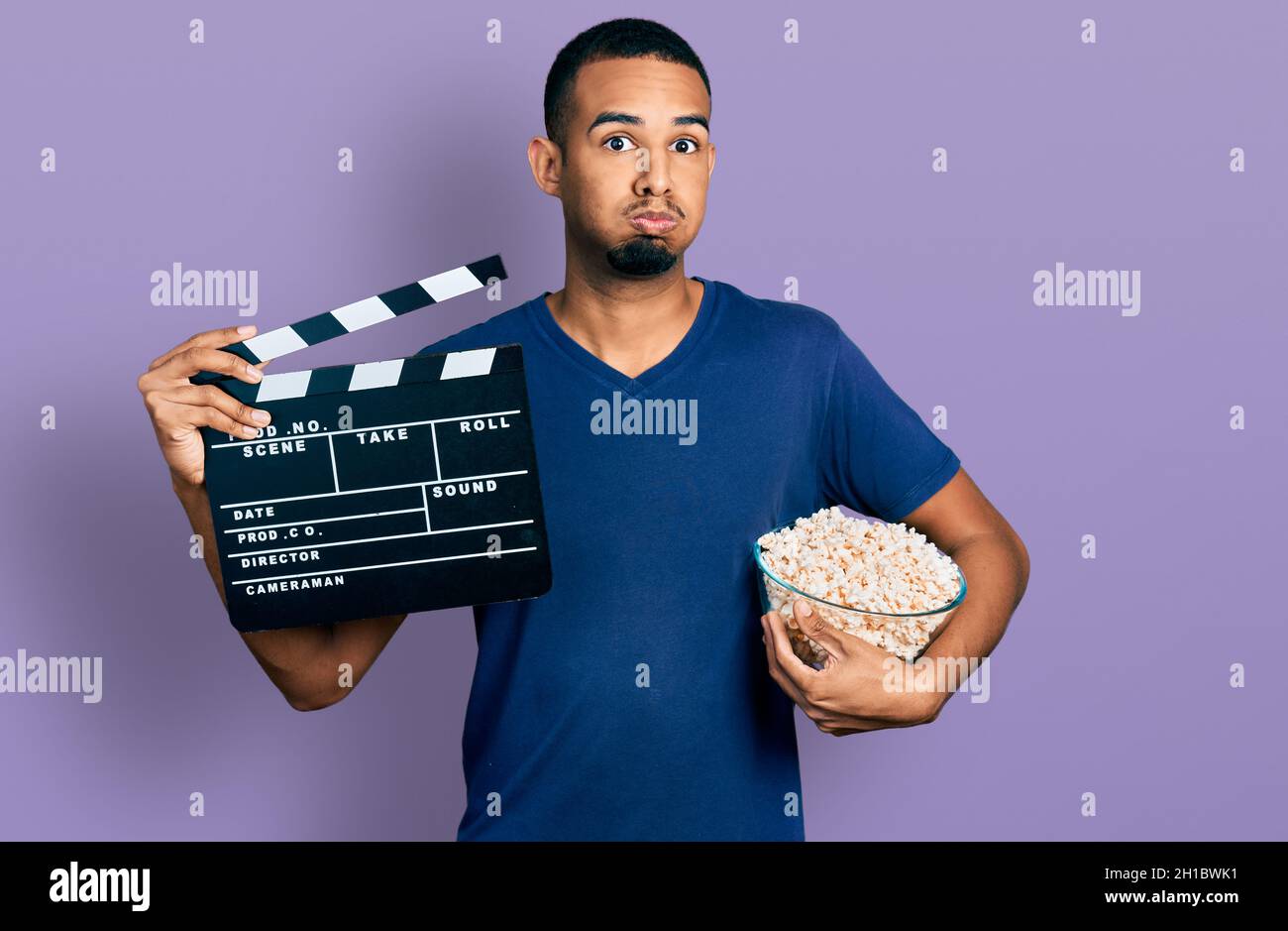 Young african american man eating popcorn holding film clapboard ...