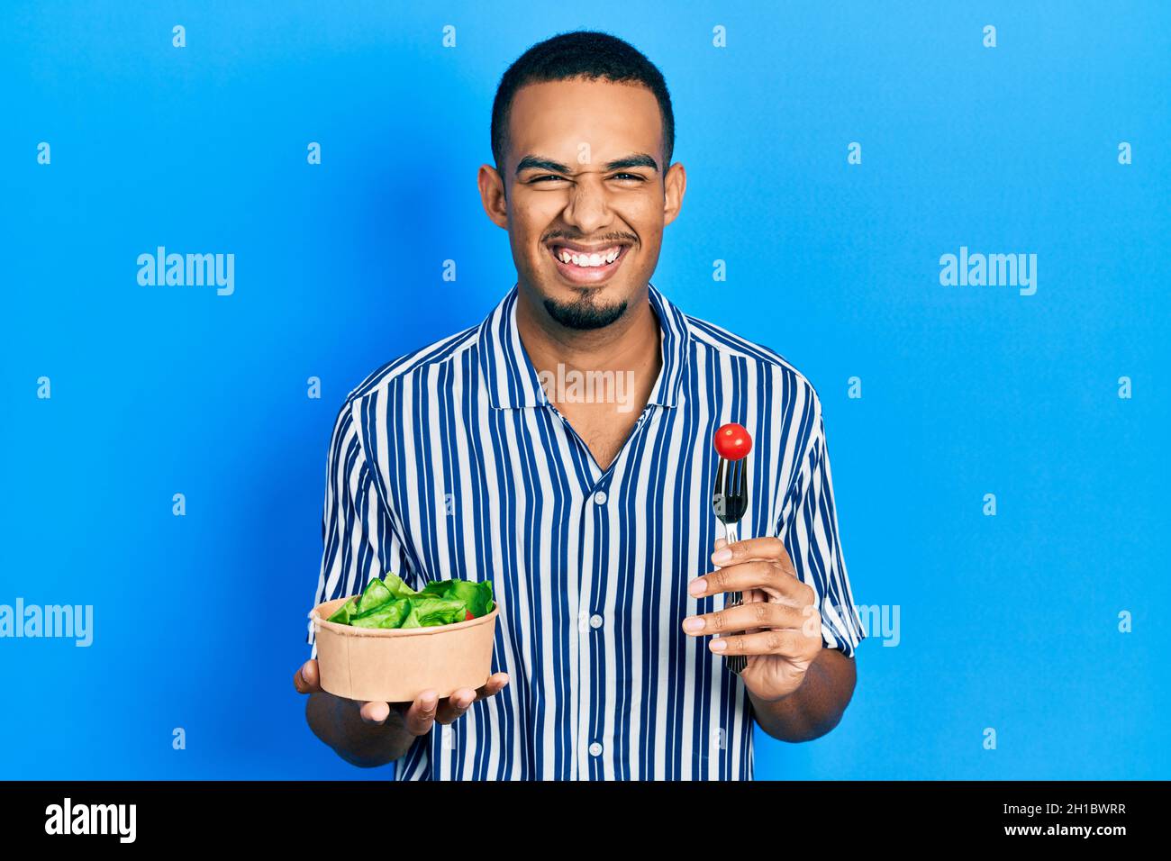 Young african american man eating salad smiling and laughing hard out ...