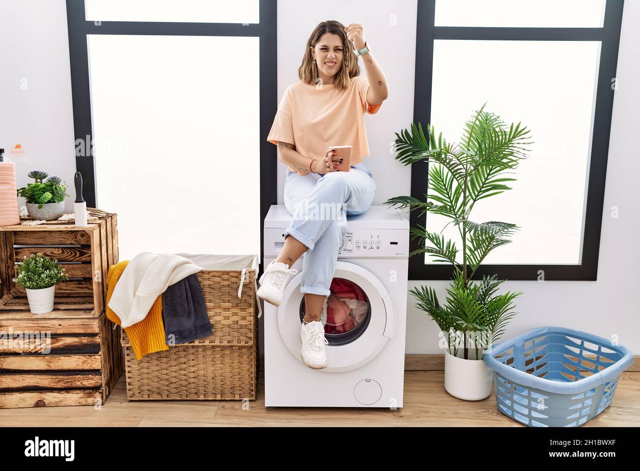 Young hispanic woman drinking coffee waiting for washing machine at ...