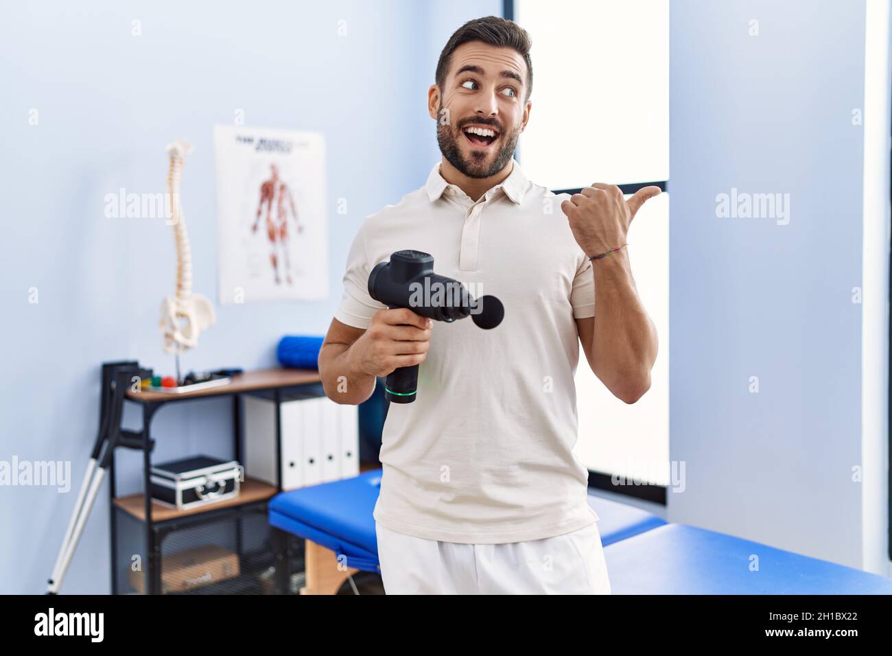 Handsome hispanic man holding therapy massage gun at physiotherapy ...