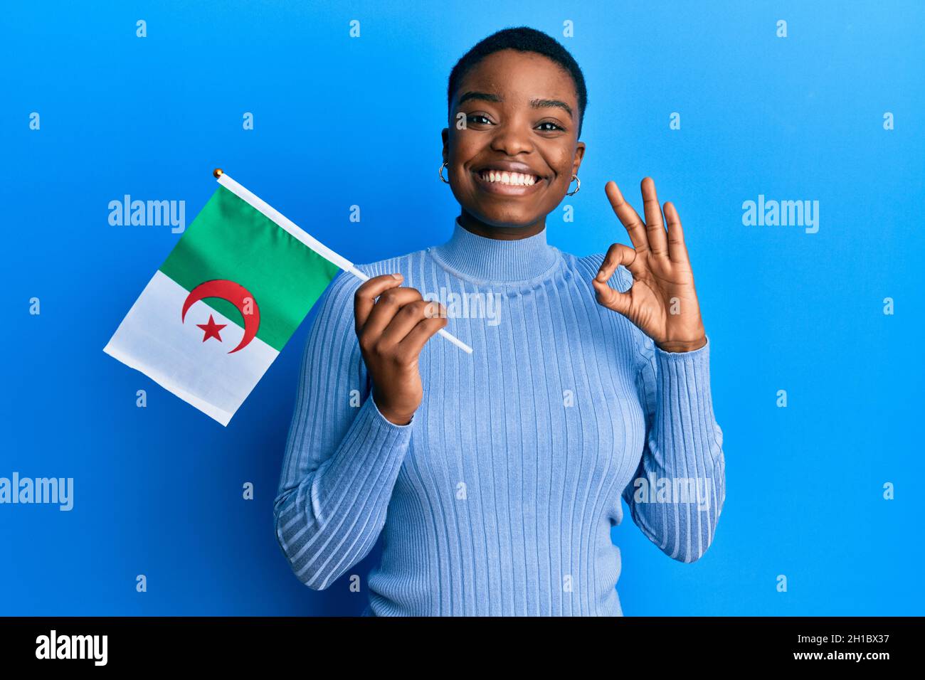 Young african american woman holding algeria flag doing ok sign with ...