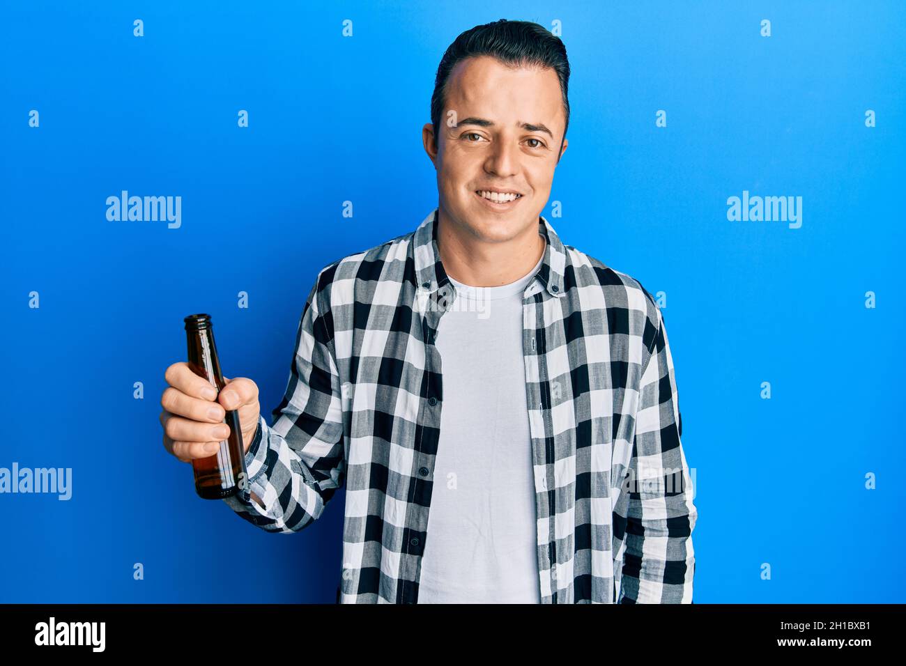 Handsome young man drinking a pint of beer looking positive and happy ...
