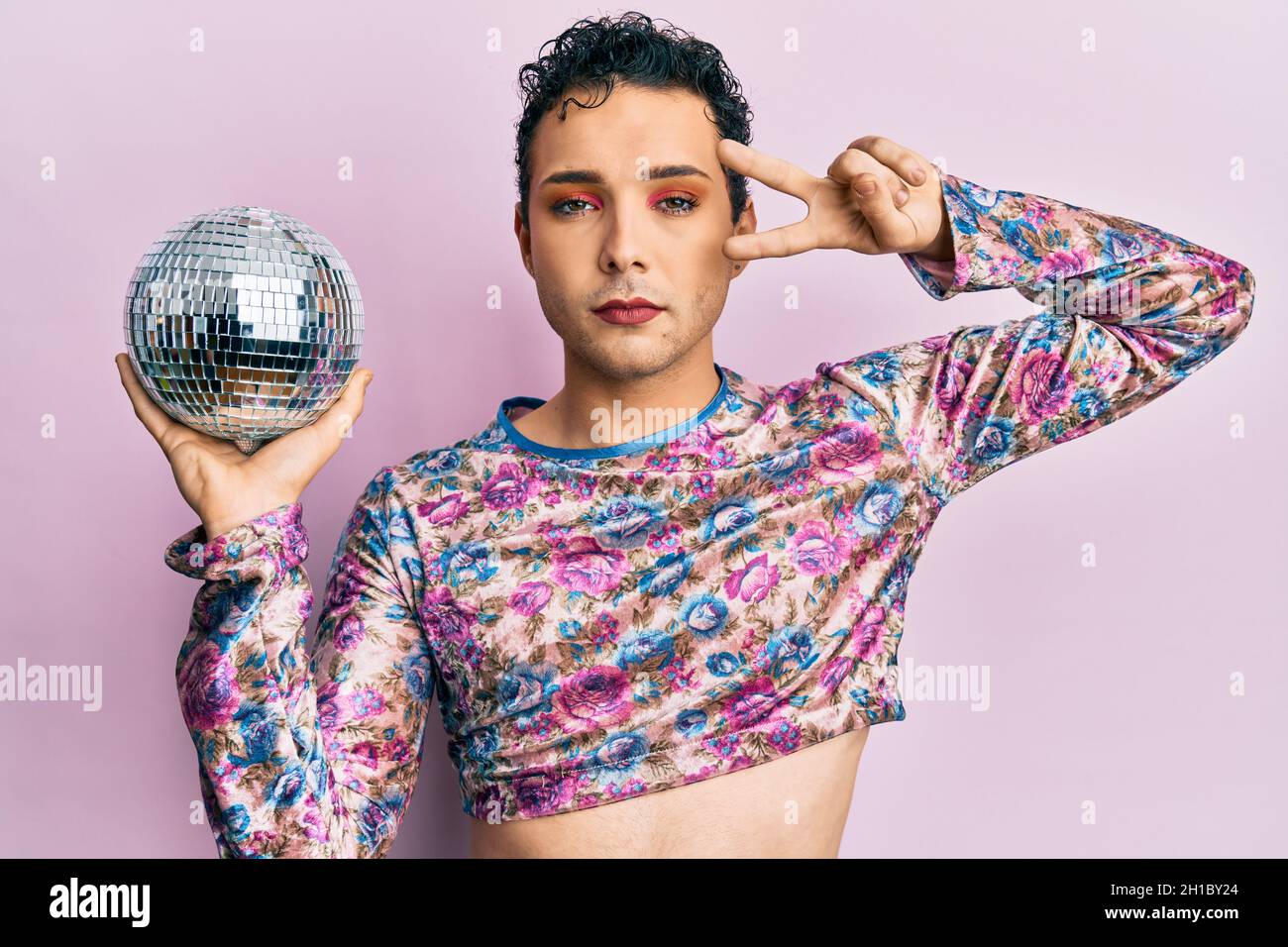 Handsome man wearing make up holding shiny disco ball relaxed with ...