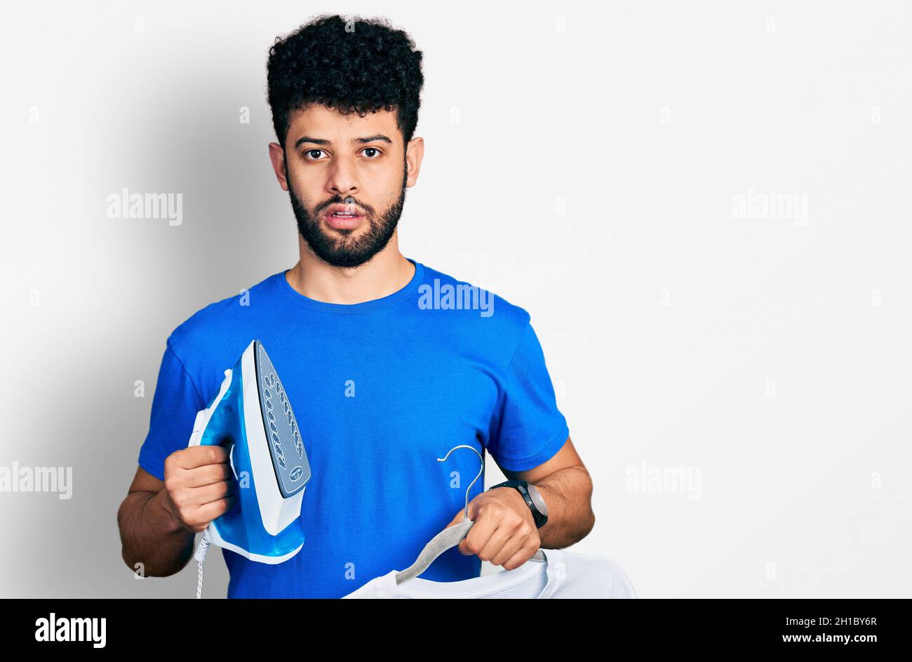 Young arab man with beard holding electric steam iron and white t shirt ...