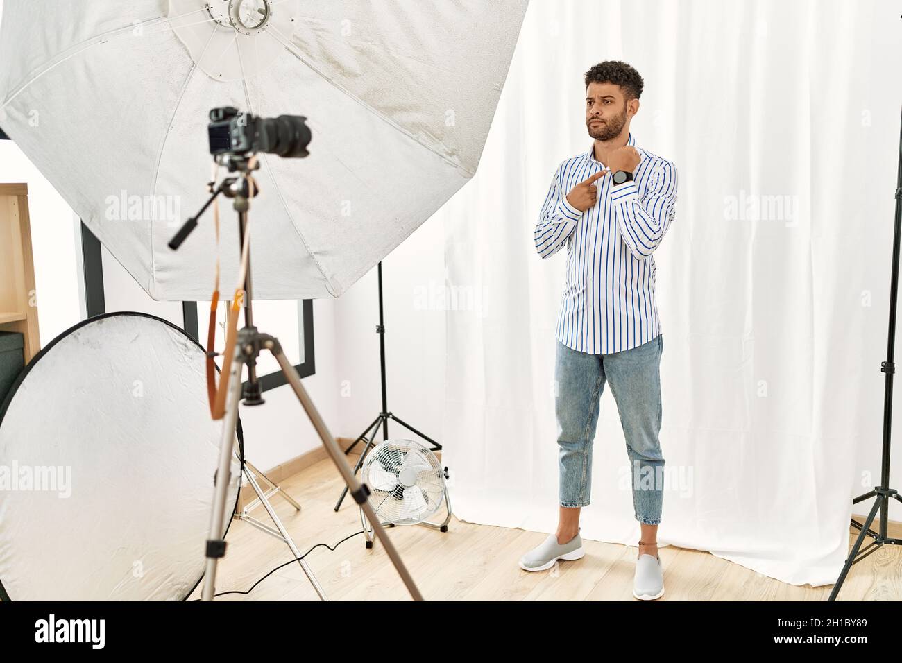 Arab young man posing as model at photography studio in hurry pointing ...