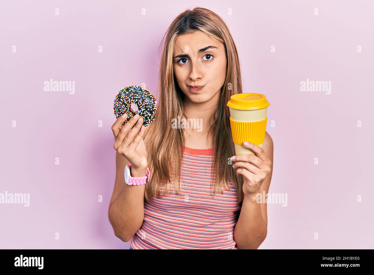 Beautiful hispanic woman eating doughnut and drinking coffee skeptic ...