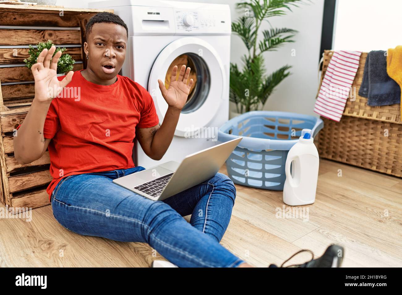 Young african man doing laundry and using computer afraid and terrified ...