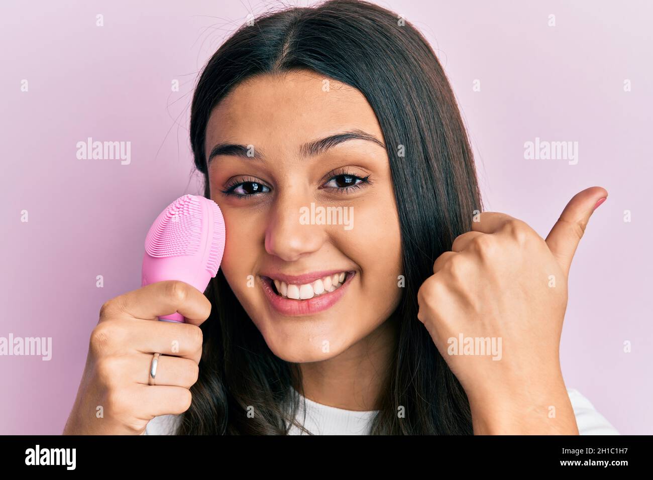 Young hispanic woman using facial exfoliating cleaner pointing thumb up ...