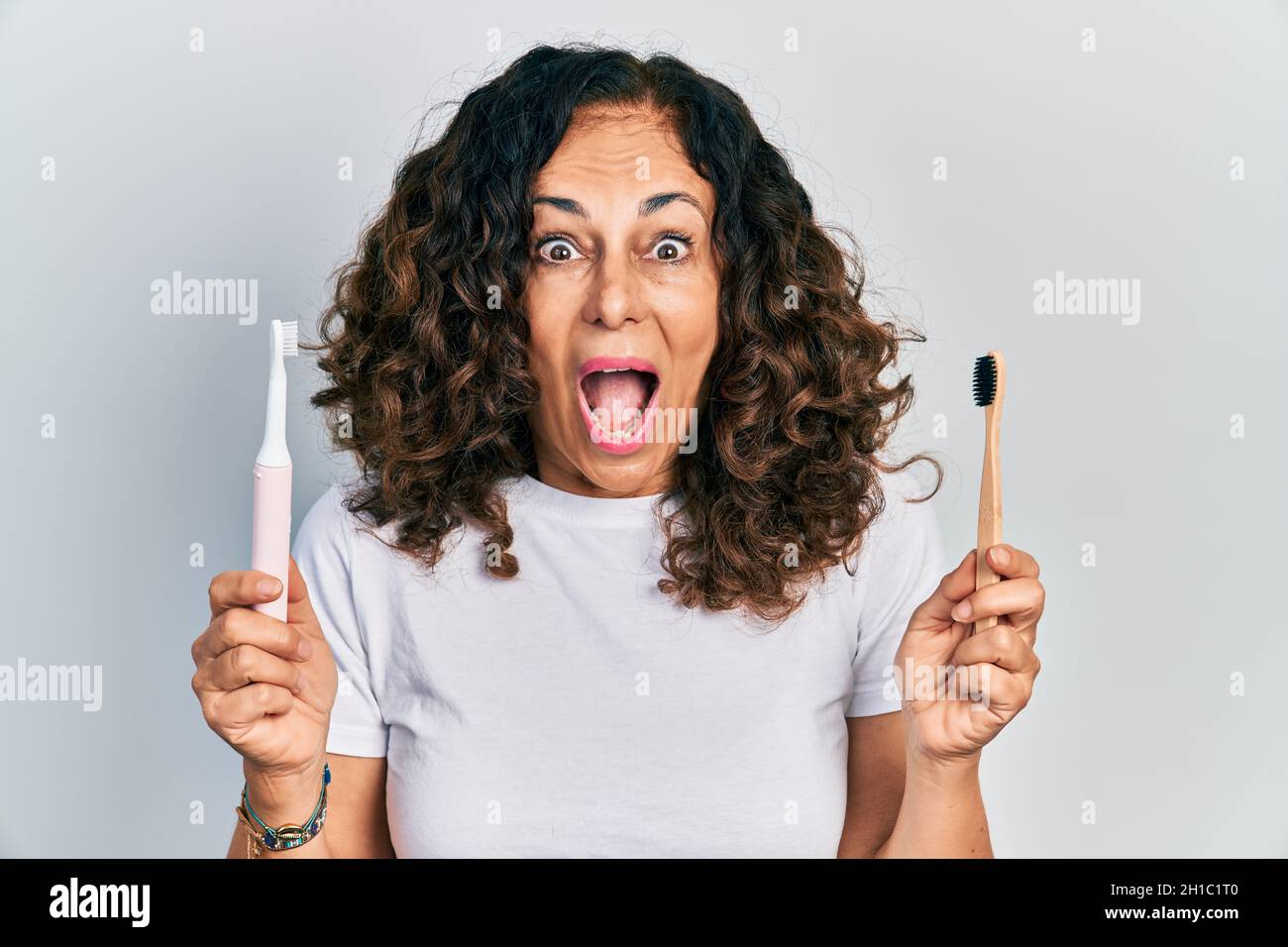 Middle age hispanic woman holding electric toothbrush and teethbrush ...