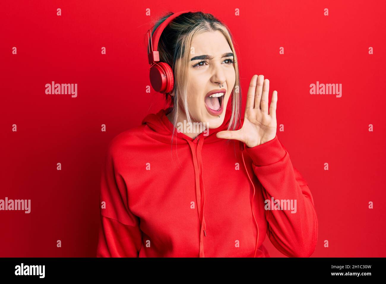 Young modern girl wearing gym clothes and using headphones shouting and ...