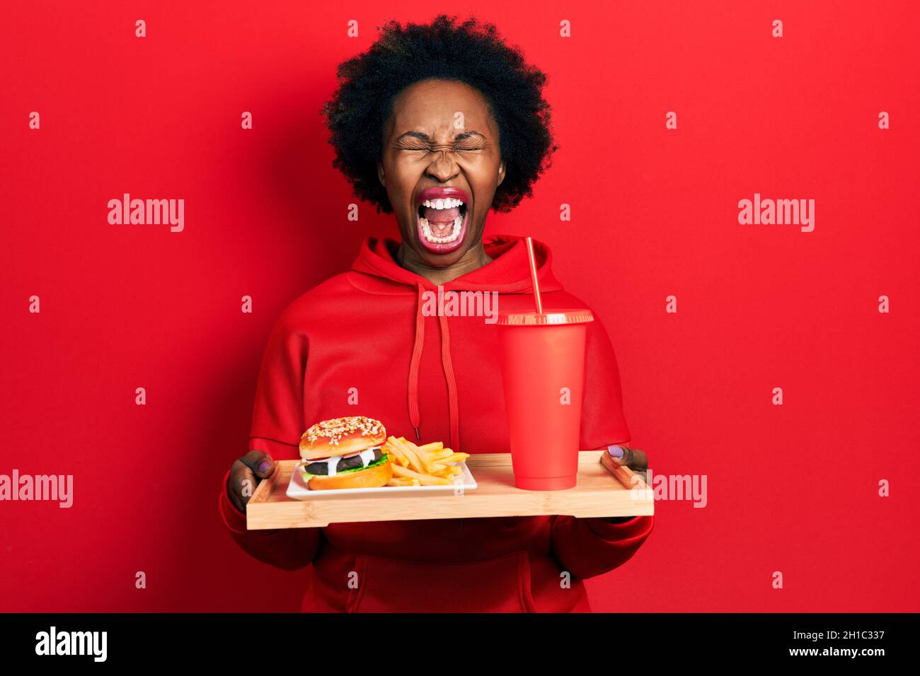 Young african american woman eating a tasty classic burger with fries ...