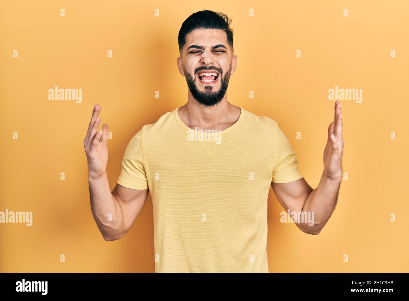 Handsome man with beard wearing casual yellow t shirt celebrating mad ...