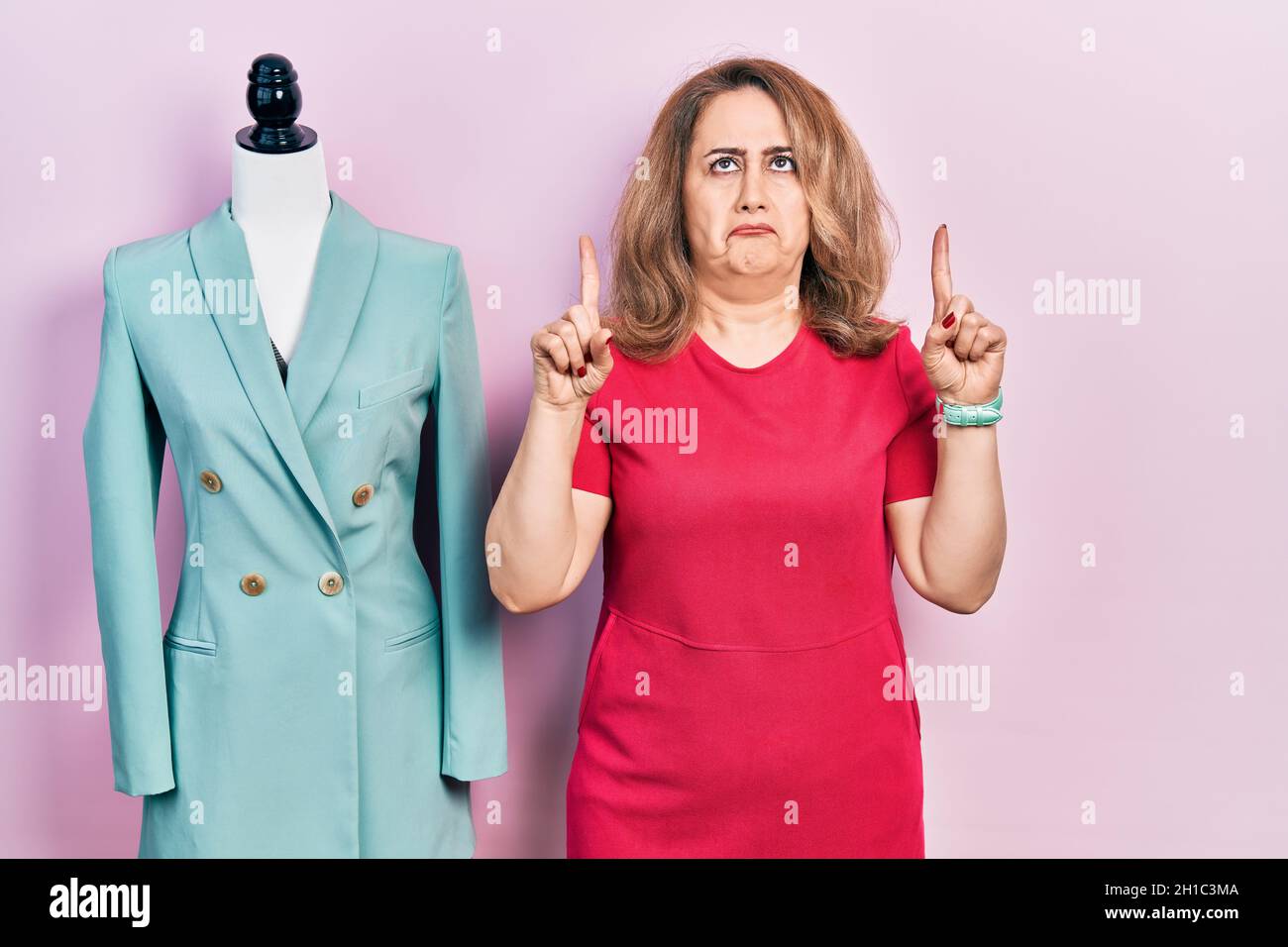 Middle age caucasian woman standing by manikin pointing up looking sad ...