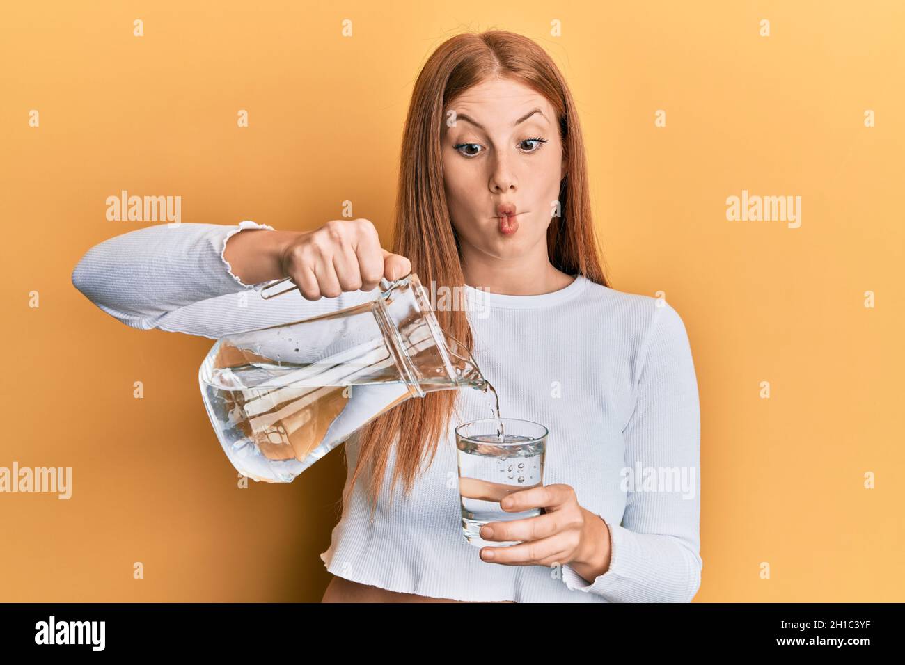 Young irish woman pouring water making fish face with mouth and ...
